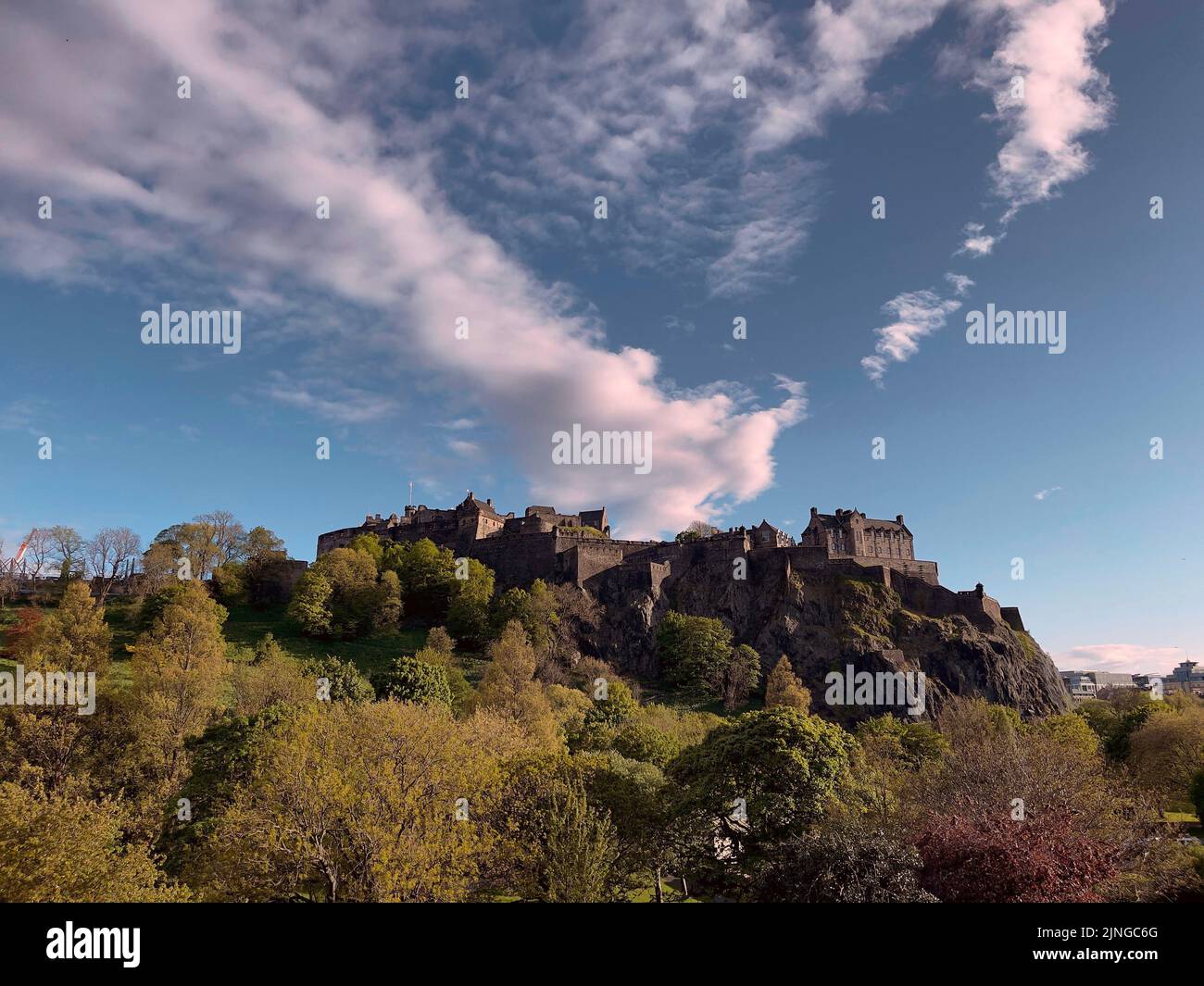 The Edinburgh Castle surrounded by lush greenery against blue cloudy ...