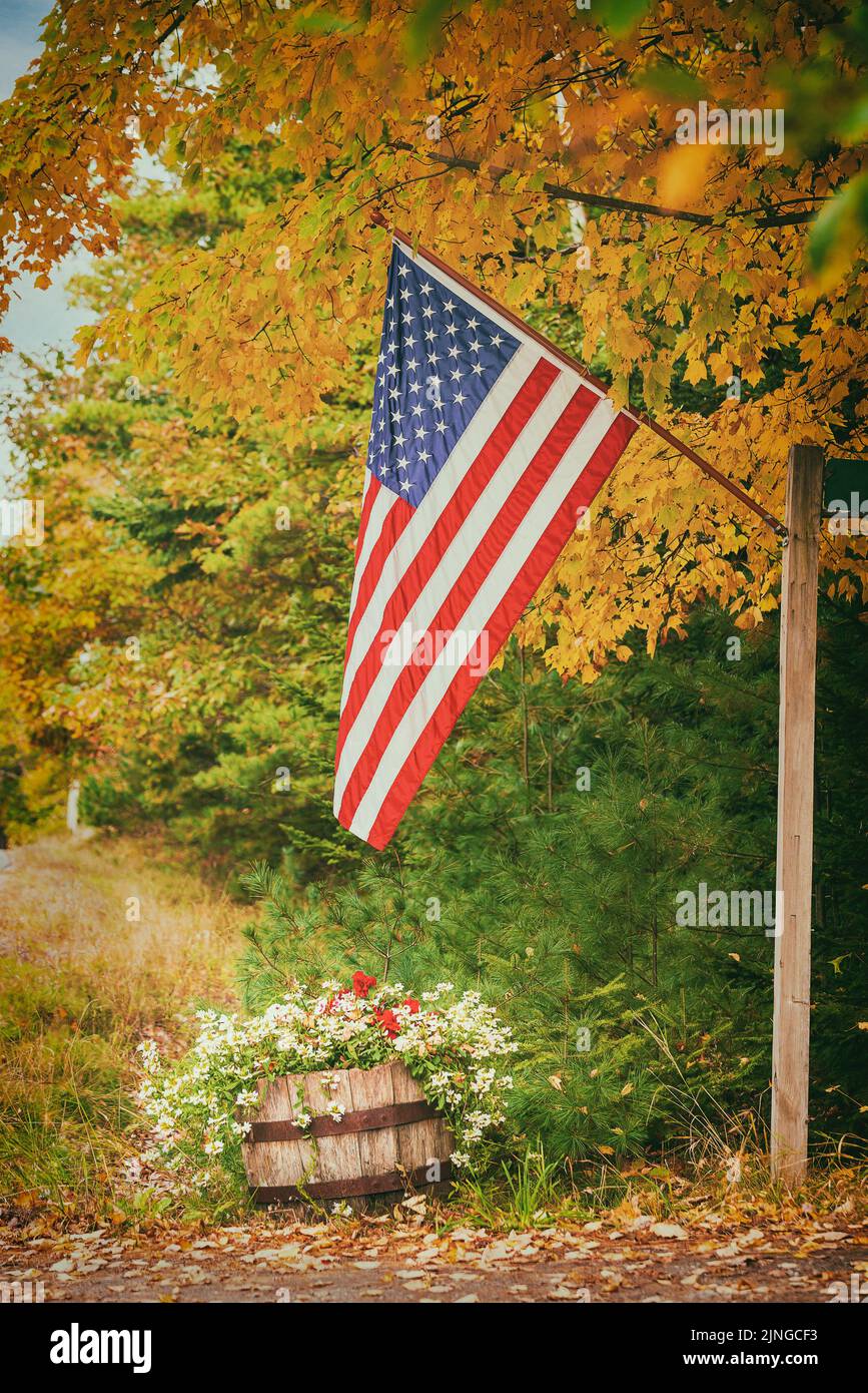 American flag hanging on the roadside against golden autumn foliage and ...