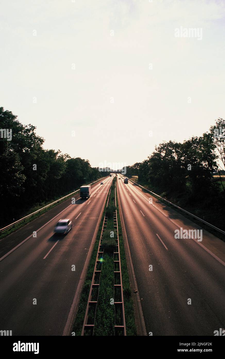 A vertical shot of a two lane freeway with cars surrounded by trees on ...
