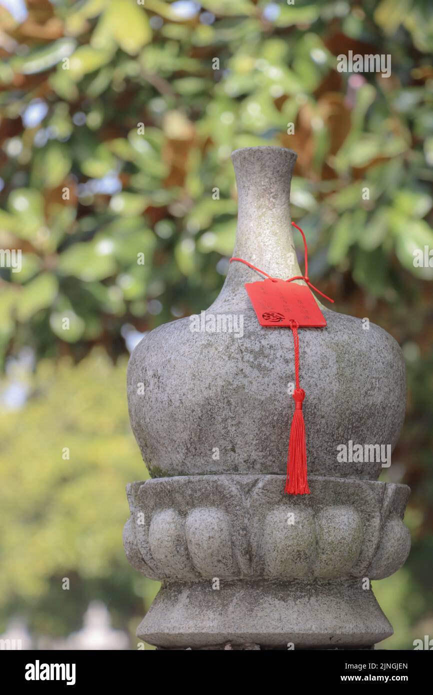 A vertical shot of a garden stone lantern with a red charm hanging on ...