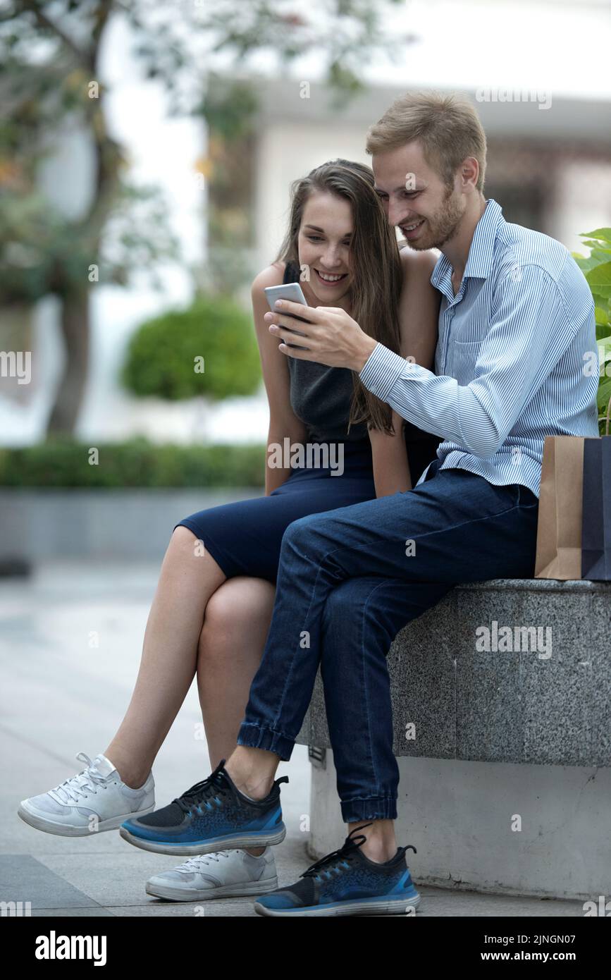 Cheerful couple using smartphone application together after shopping ...
