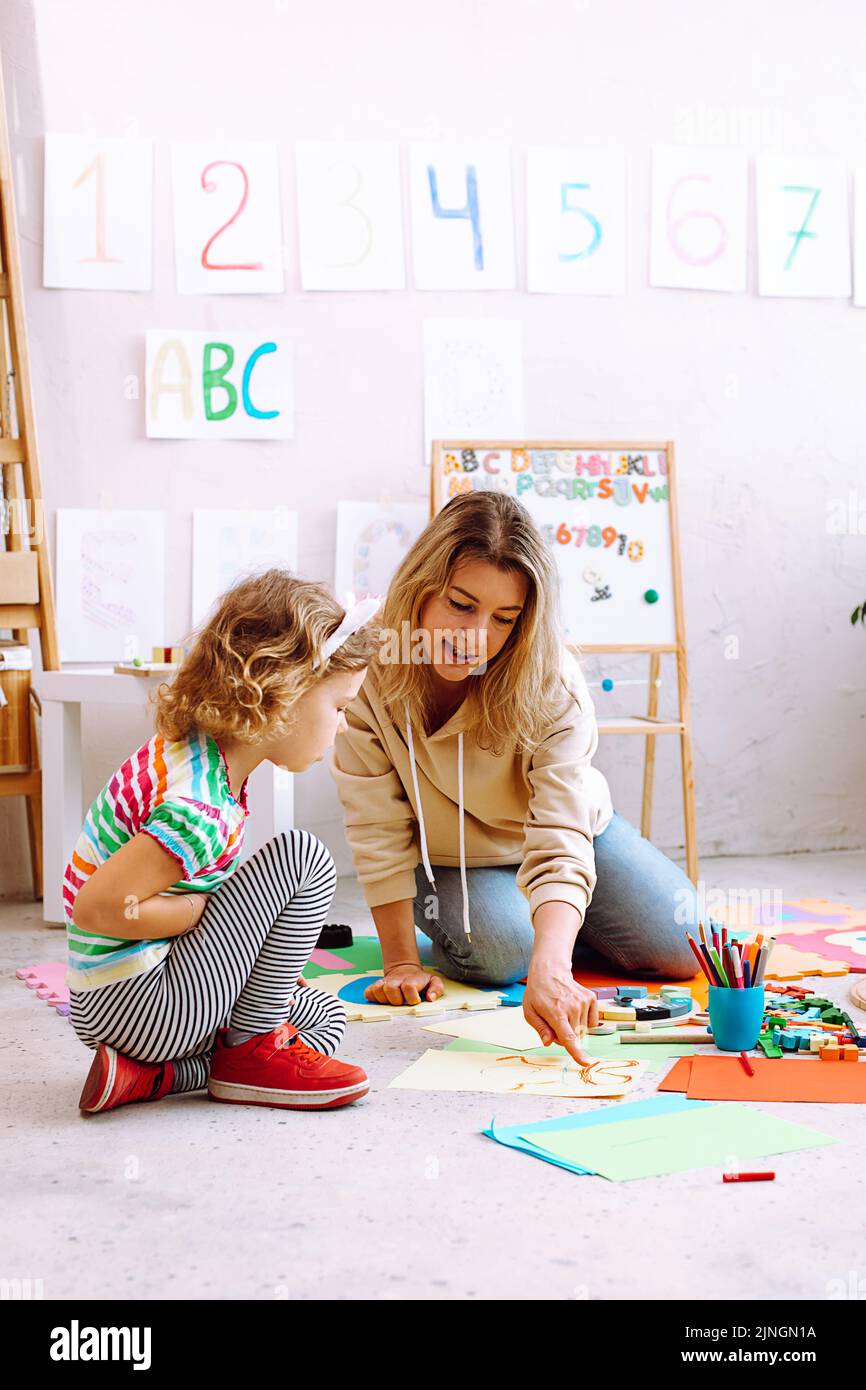 Portrait of curious little girl sit with young smiling woman teacher ...