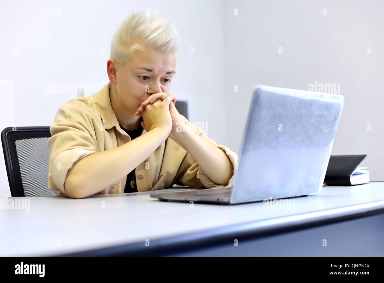 Girl with short blonde hair sitting at laptop with worried face ...
