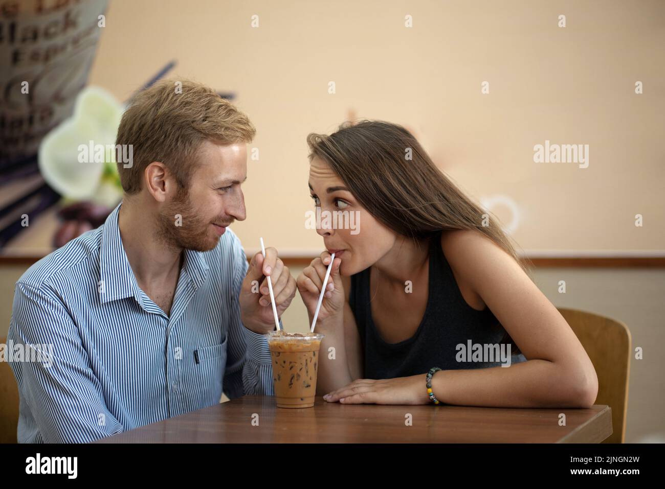 Young couple drinkink milkshake through straws from one plastic cup ...