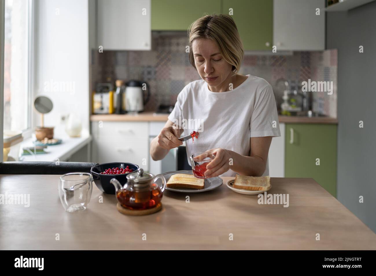 Pensive middle-aged woman sits alone at kitchen table eating healthy ...