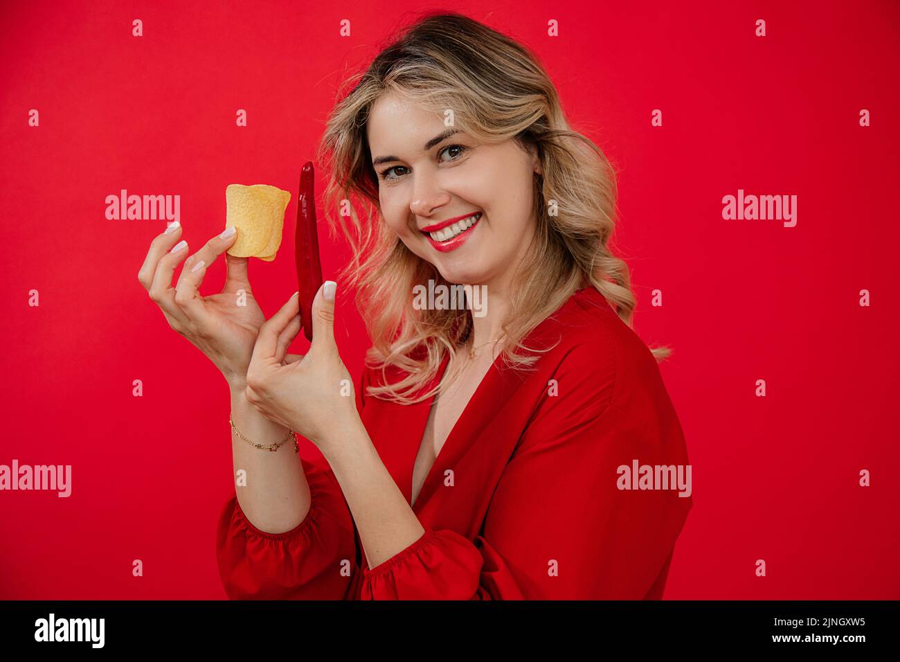 Smiling pleased blonde woman showing junk chili pepper and yummy salty ...