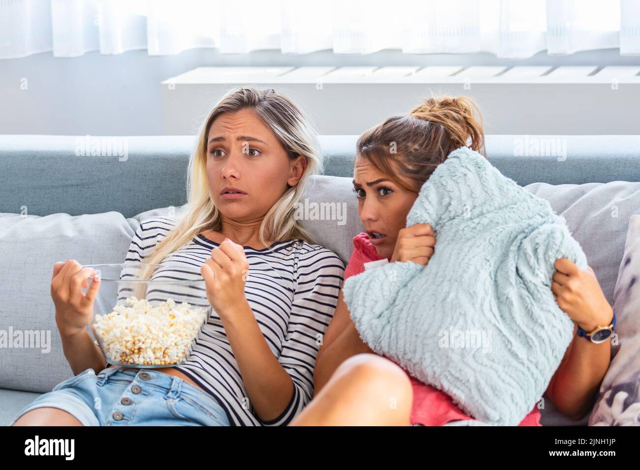 Terrified friends watching tv in the night sitting on a couch in the ...