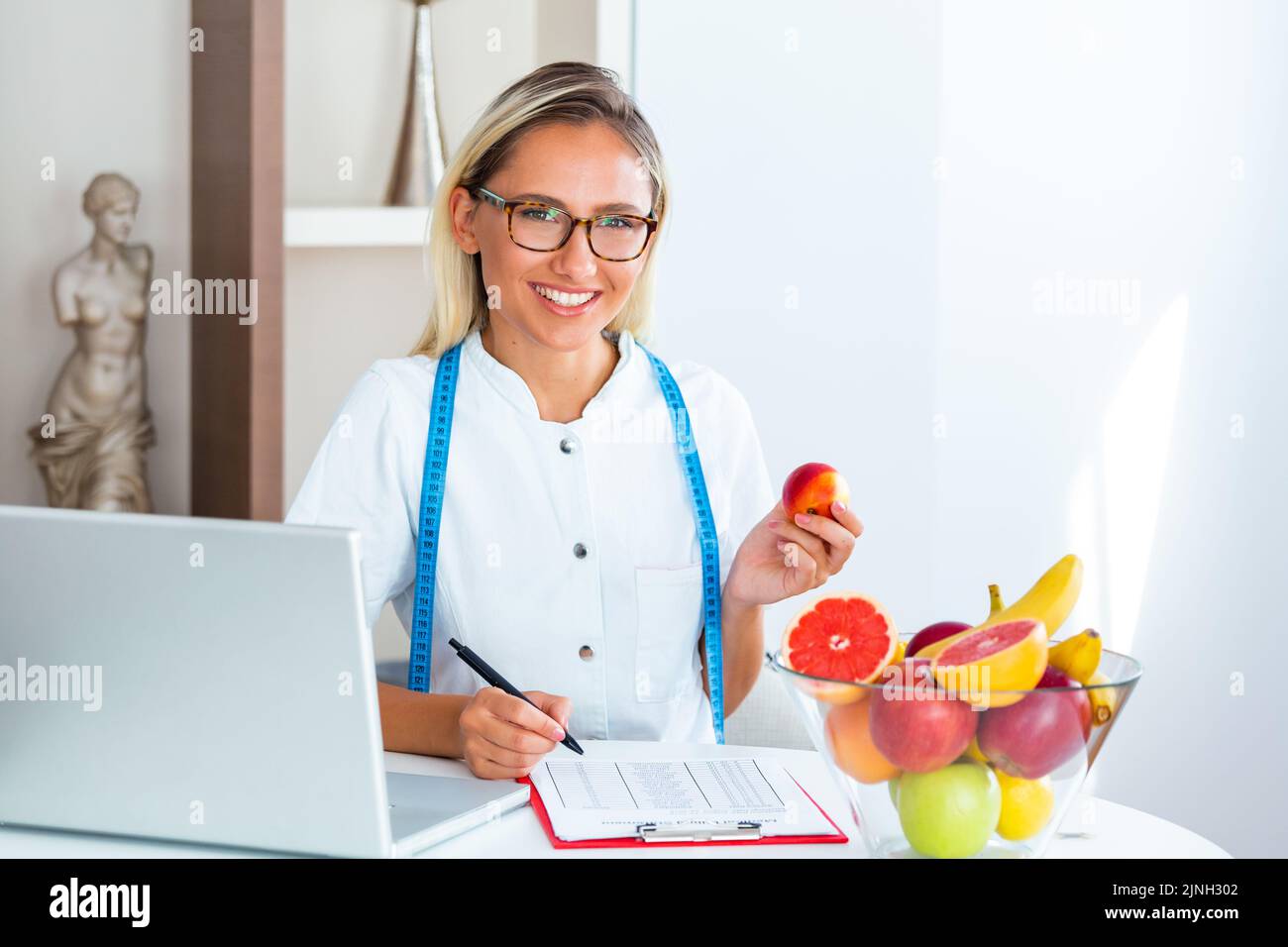Smiling nutritionist in her office, she is showing healthy vegetables ...