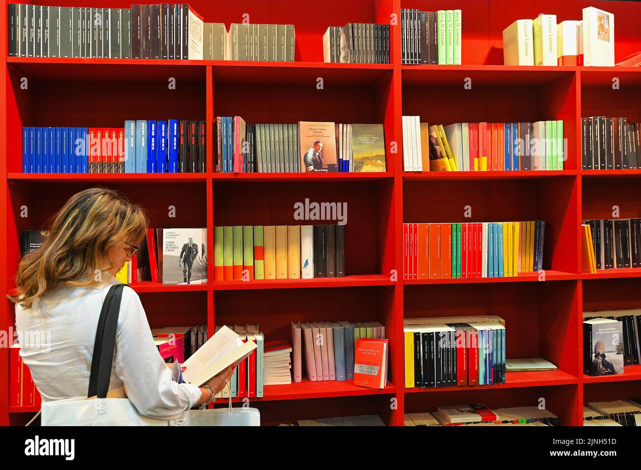 A back view of a woman reading a book at a bookshop in front of red ...