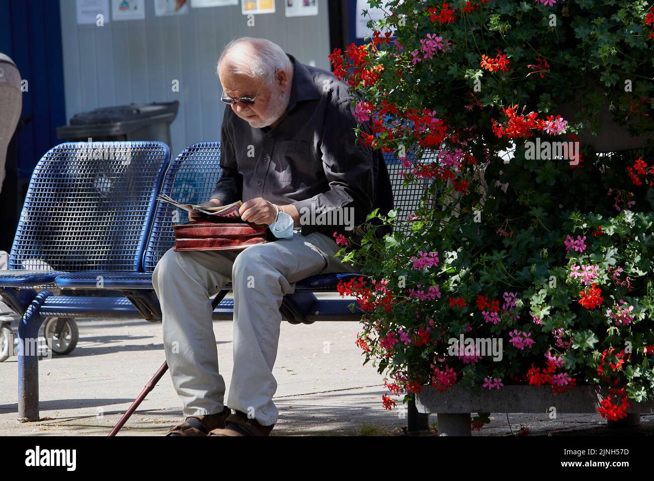 An old man in sunglasses reading a magazine on a bench in Heinsberg ...