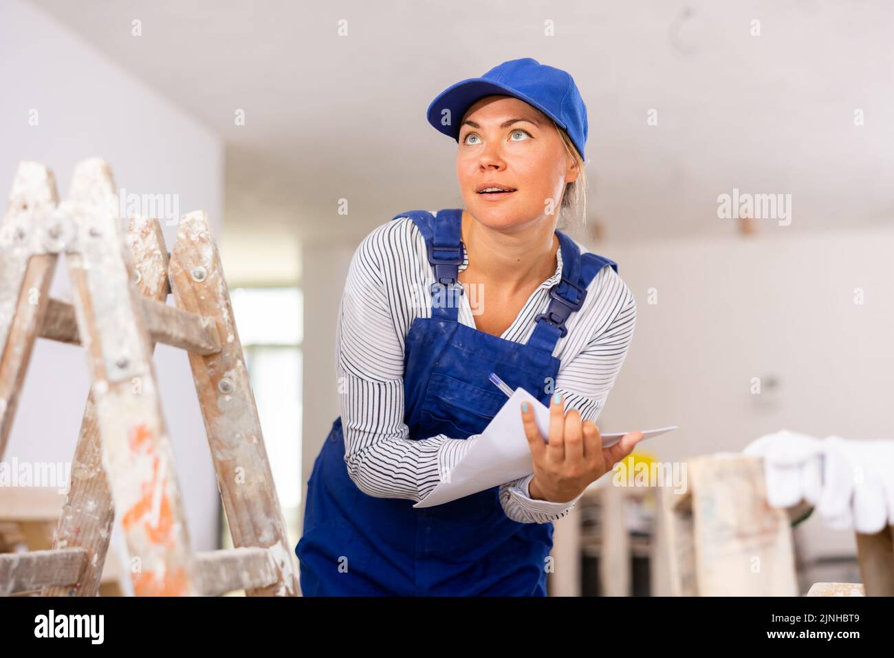 Female designer in blue overalls making checklist while planning ...