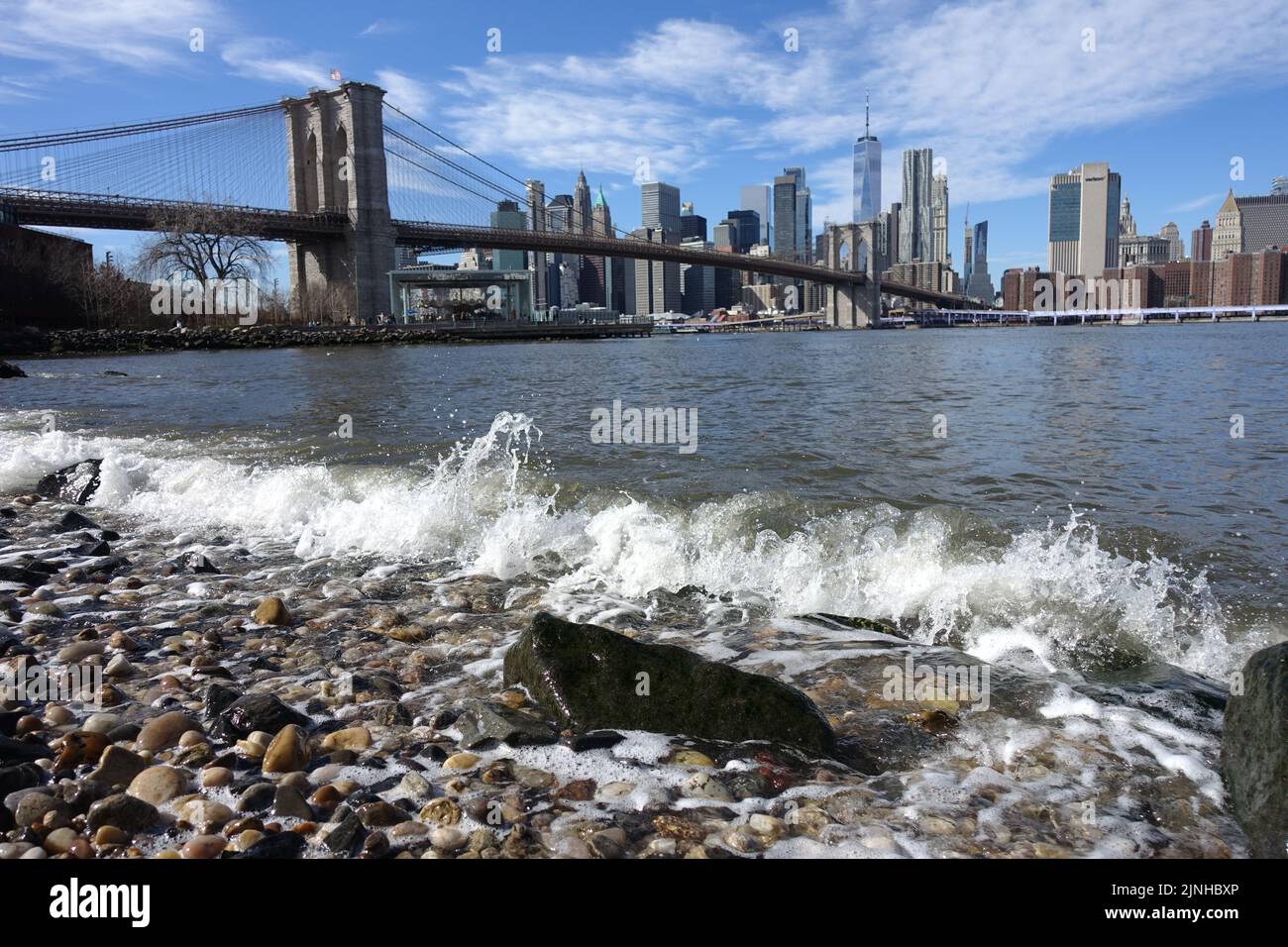 The NYC skyline view from the Pebble Beach with the Brooklyn Bridge in ...