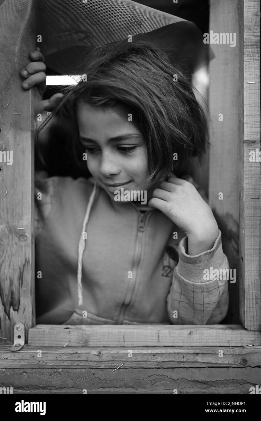 A vertical grayscale shot of a smiling little refugee girl in a camp in ...