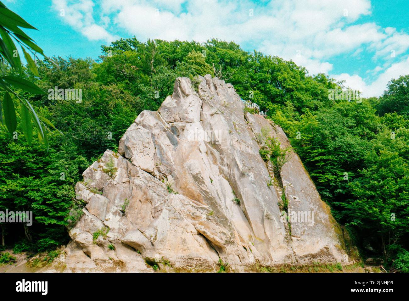 Large rock with green forest around Stock Photo - Alamy