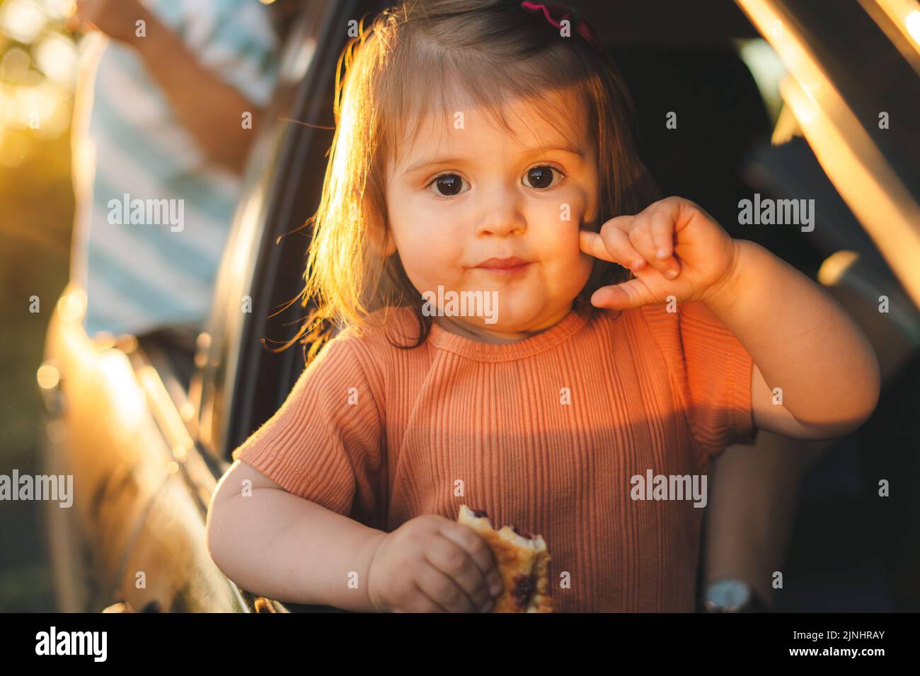 Baby girl in the car looking throw window while eating tasty pie ...