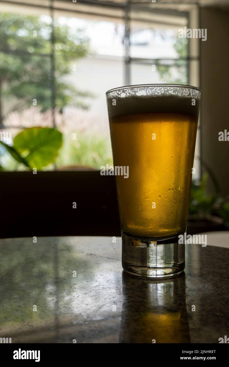 glass of beer on a terrazzo table, two yellow chairs in the background ...