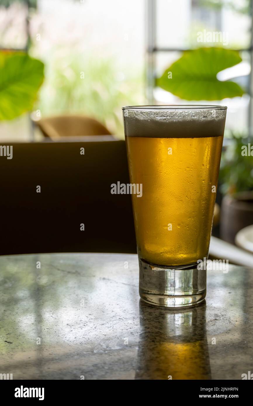 glass of beer on a terrazzo table, two yellow chairs in the background ...