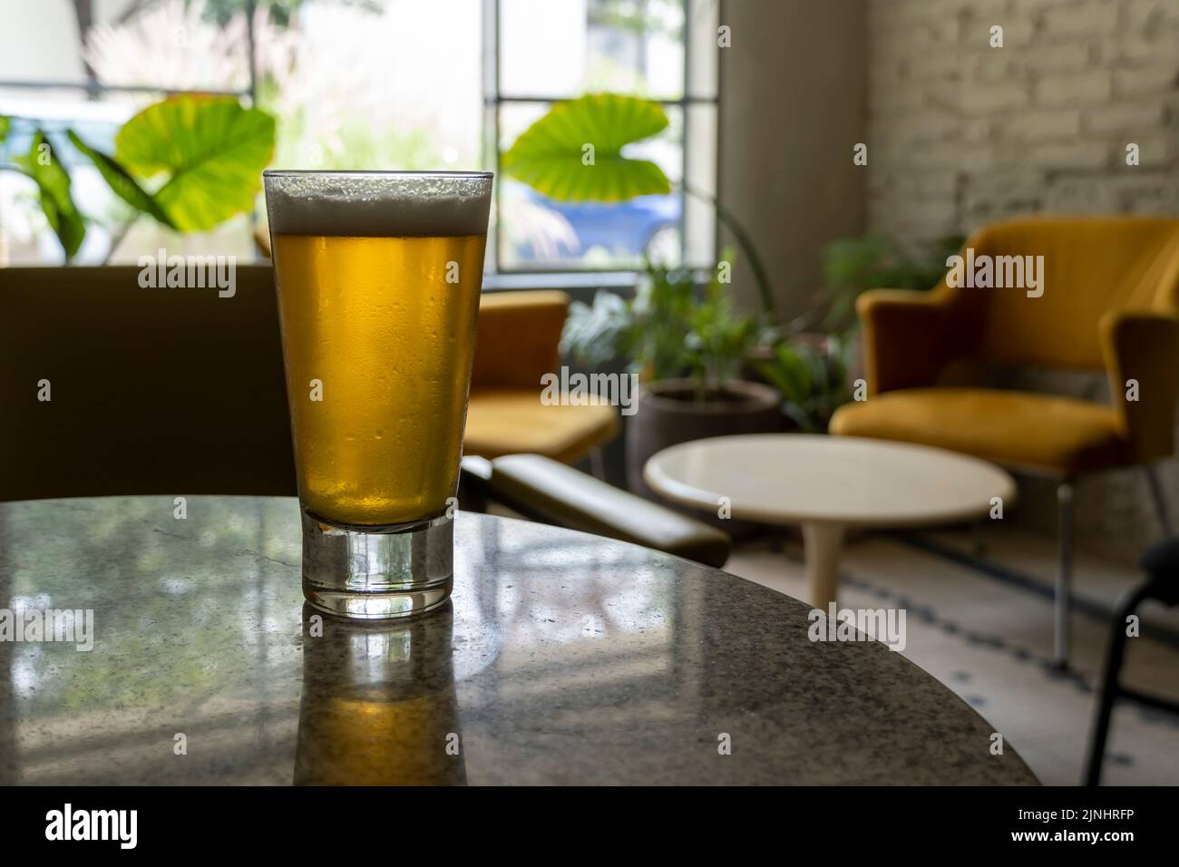 glass of beer on a terrazzo table, two yellow chairs in the background ...