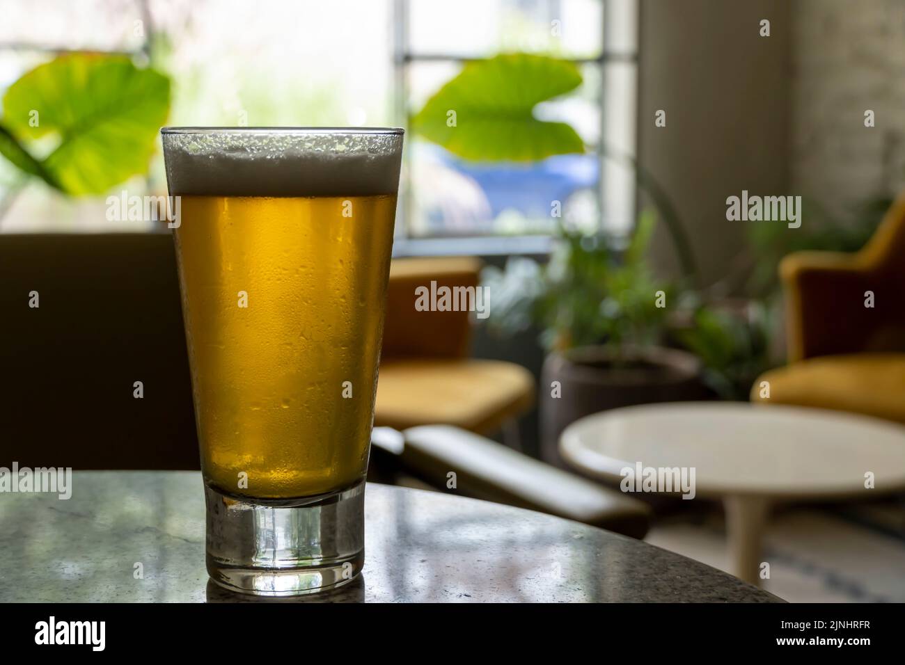 glass of beer on a terrazzo table, two yellow chairs in the background ...