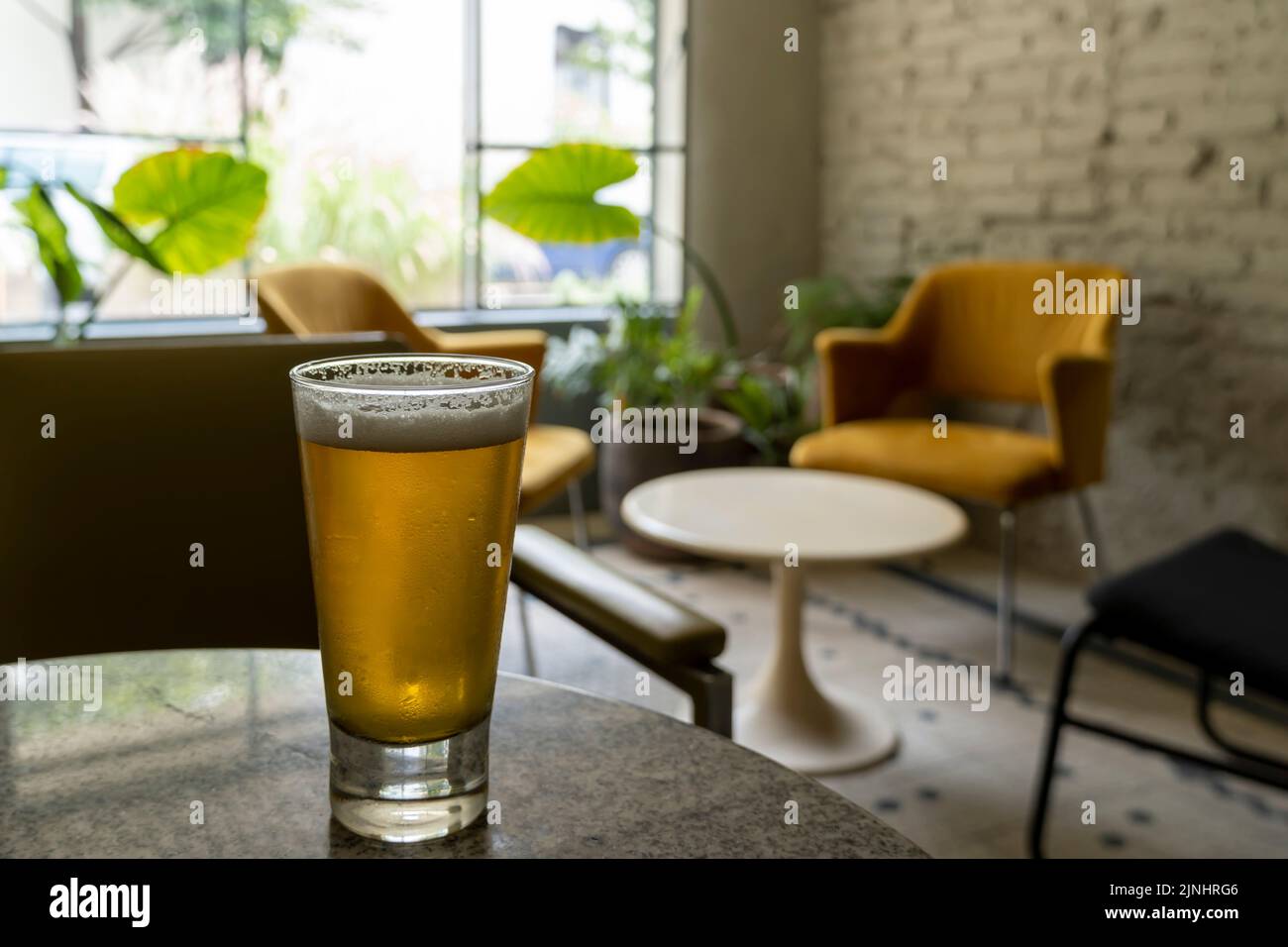 glass of beer on a terrazzo table, two yellow chairs in the background ...