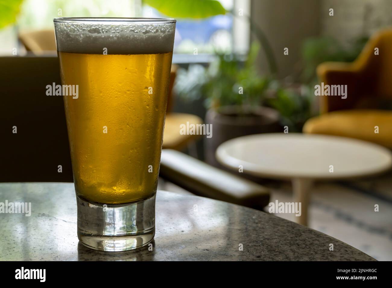 glass of beer on a terrazzo table, two yellow chairs in the background ...