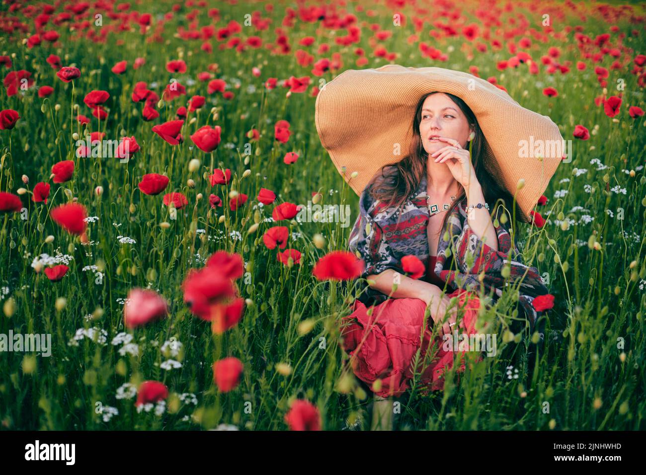 Portrait of a woman in a poppy field wearing a wide-brimmed hat at ...