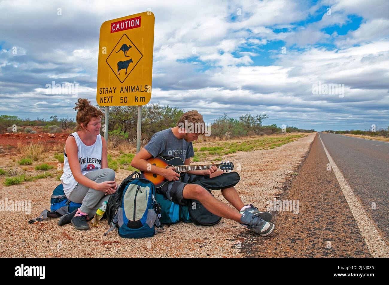 A couple of young British backpackers waiting for a lift on the highway ...