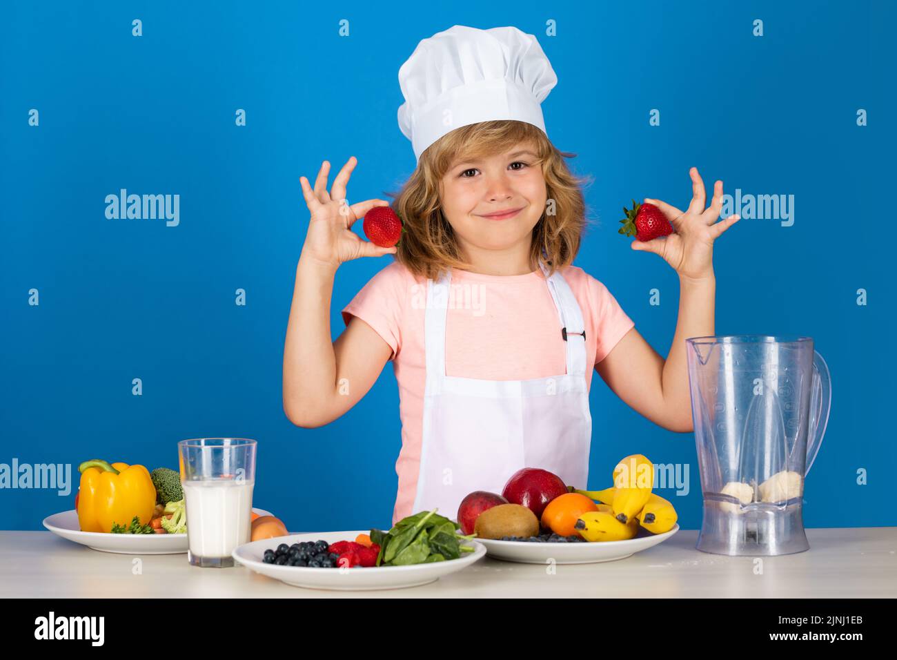 Portrait of chef child in cook hat hold strawberries. Cooking at home, kid boy preparing food ...