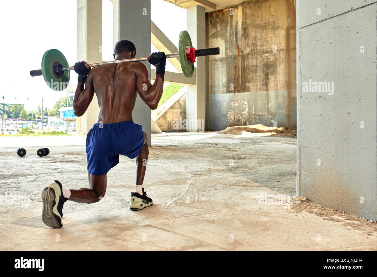 Athletic black young man lifting a heavy-weight barbell in outdoor gym ...