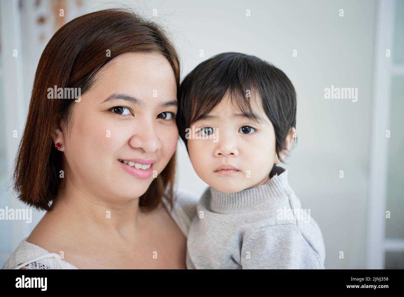 Head and shoulders portrait of beautiful Asian woman looking at camera with wide smile while ...