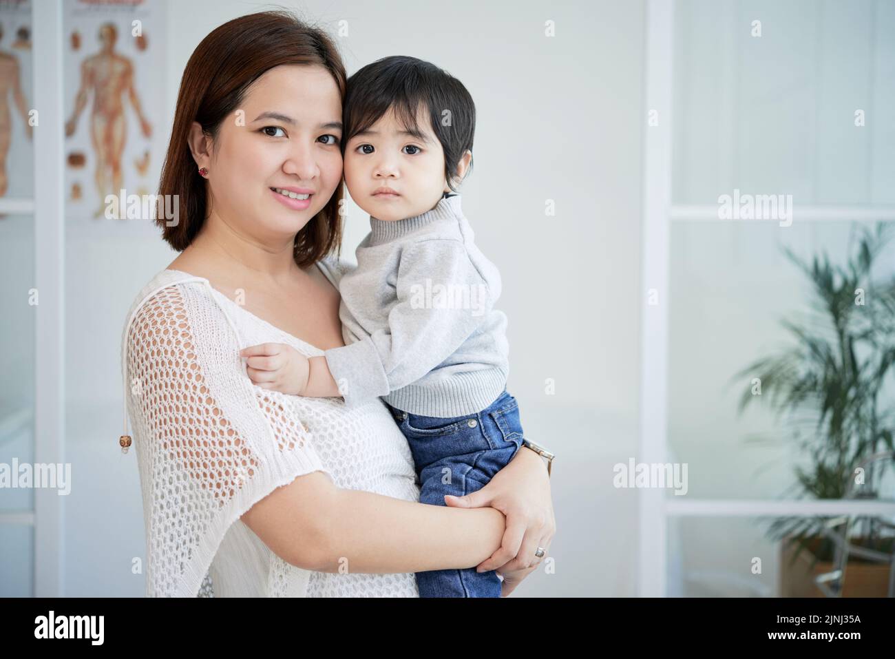 Group portrait of pretty Asian woman holding her cute little son on hands and posing for ...