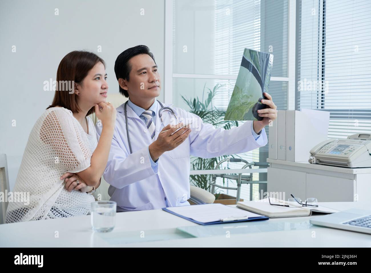 Confident middle-aged surgeon sitting at desk and explaining X-ray ...