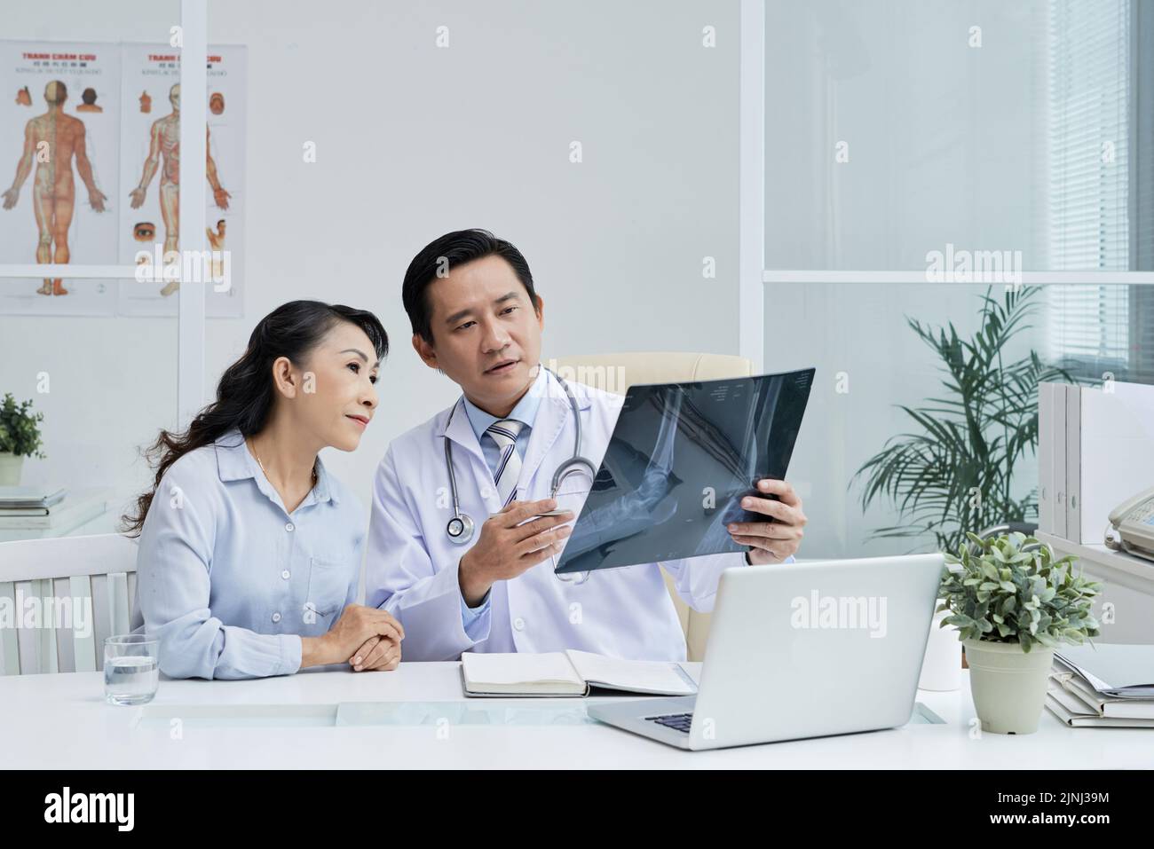 Handsome middle-aged surgeon sitting at desk and showing X-ray image to ...