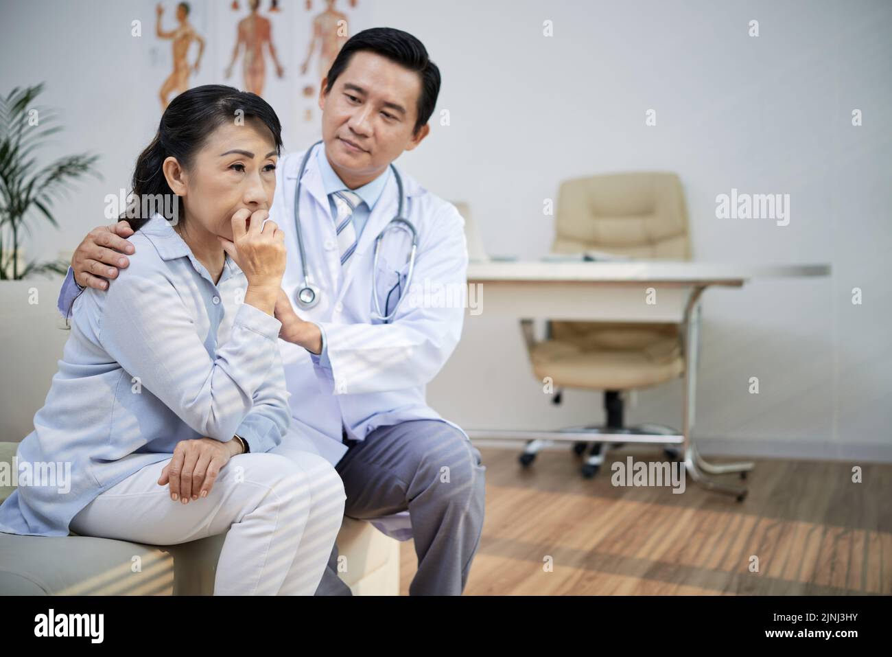 Handsome Asian physician sitting on sofa of modern office and calming ...