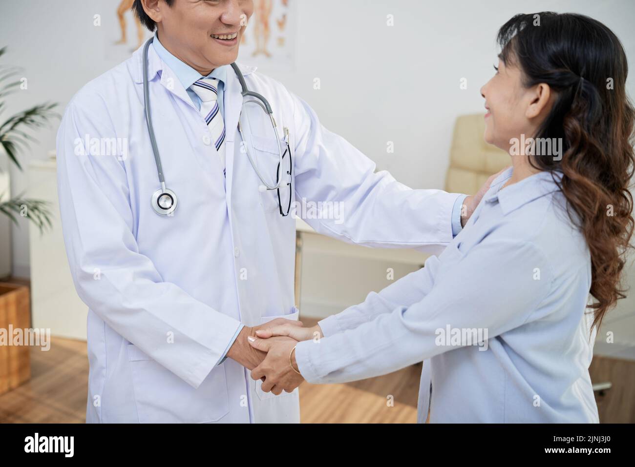 Smiling Asian patient shaking hands with highly professional doctor ...