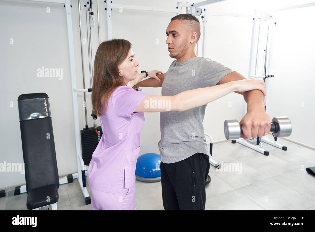 Female physiotherapist helping man to perform rehabilitation exercise ...
