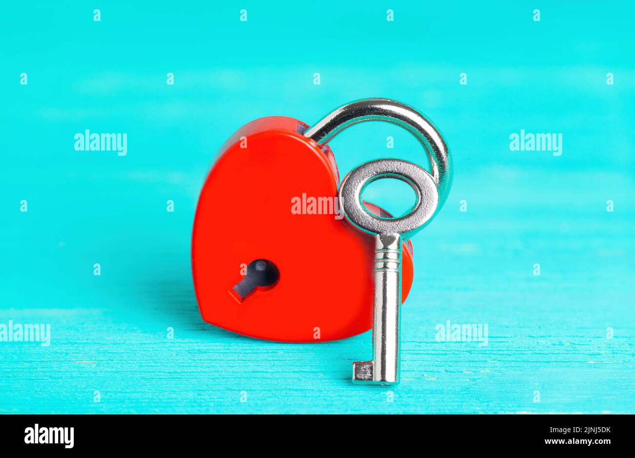 Small red heart-shaped padlock with a silver-toned master key on a blue ...