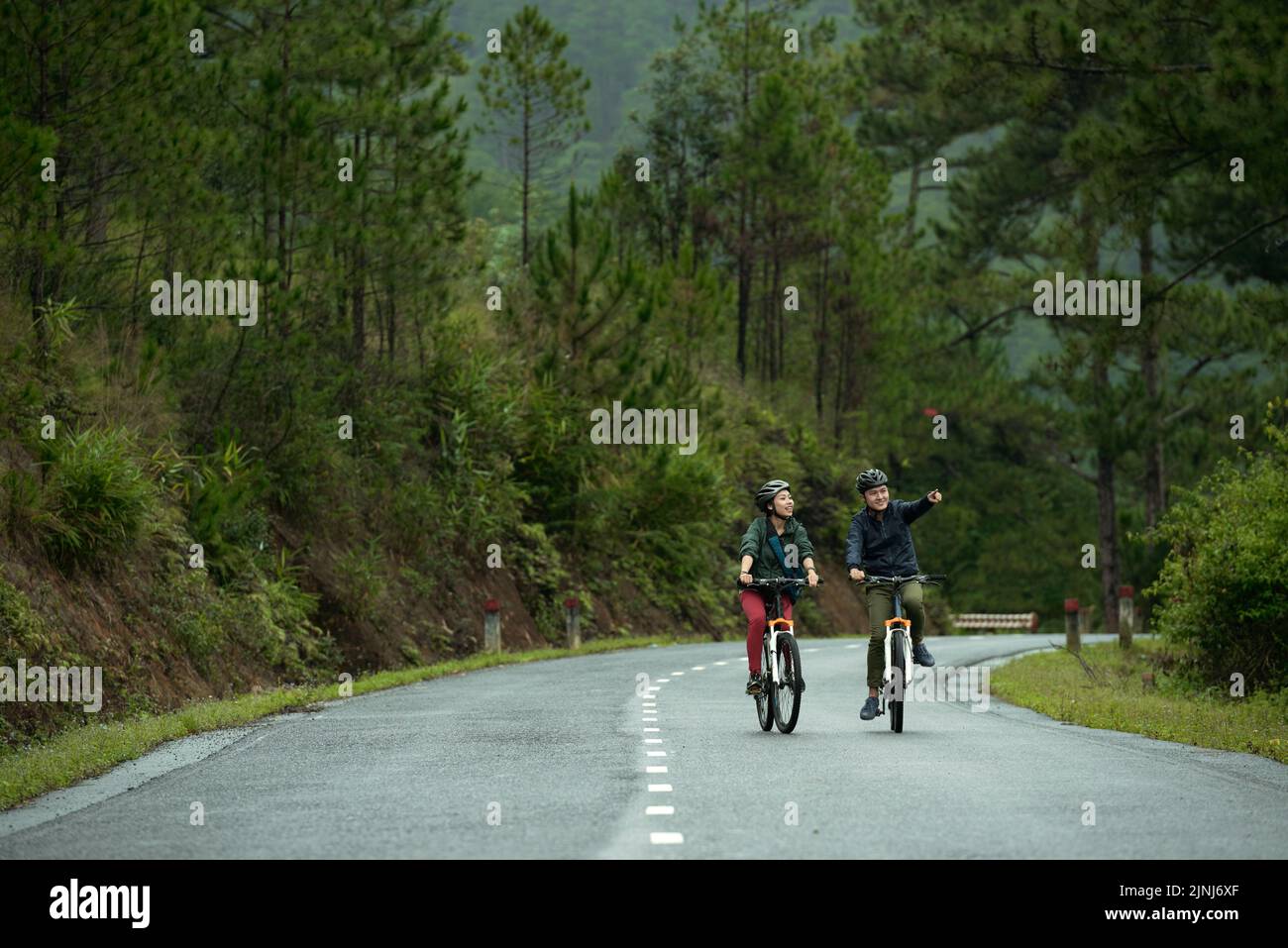 Asian couple cycling together down road, man pointing at something in ...