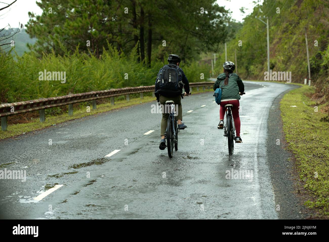 Rear view of couple cycling together down wet road, man wearing ...