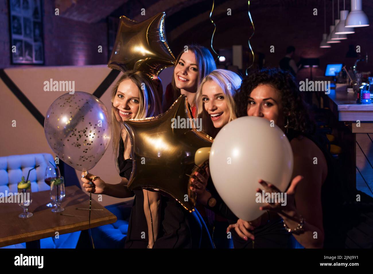 Four beautiful young Caucasian women holding balloons having night out ...
