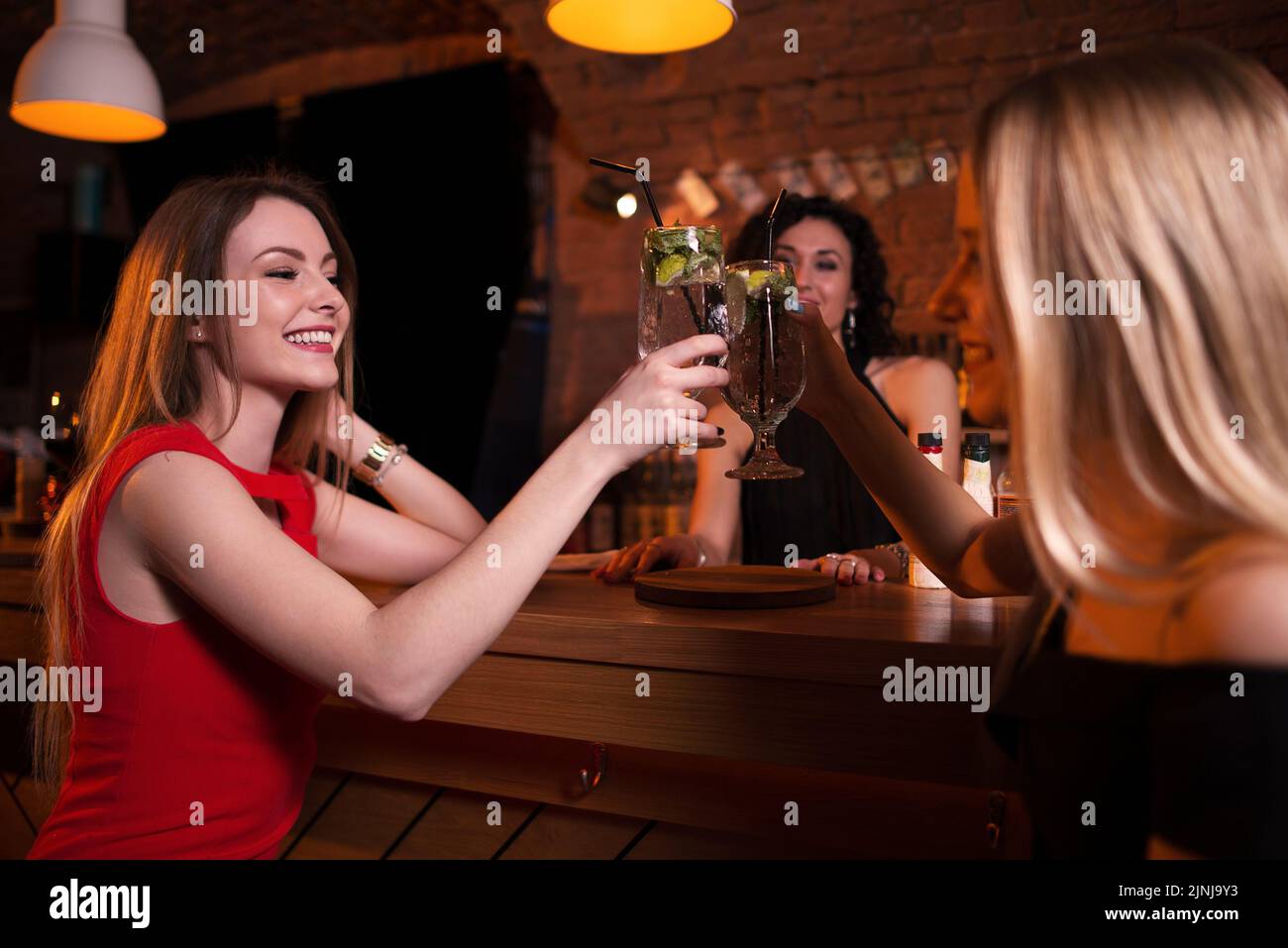 Two pretty Caucasian girls toasting drinking cocktails in pub ...