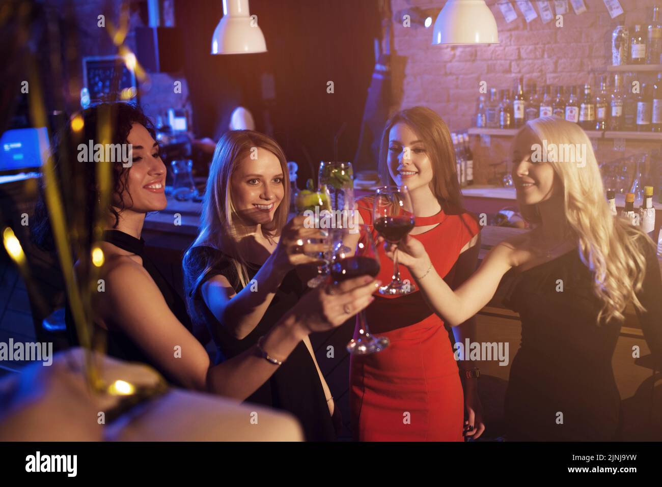 Happy young women with glasses of wine and cocktails enjoying a night ...