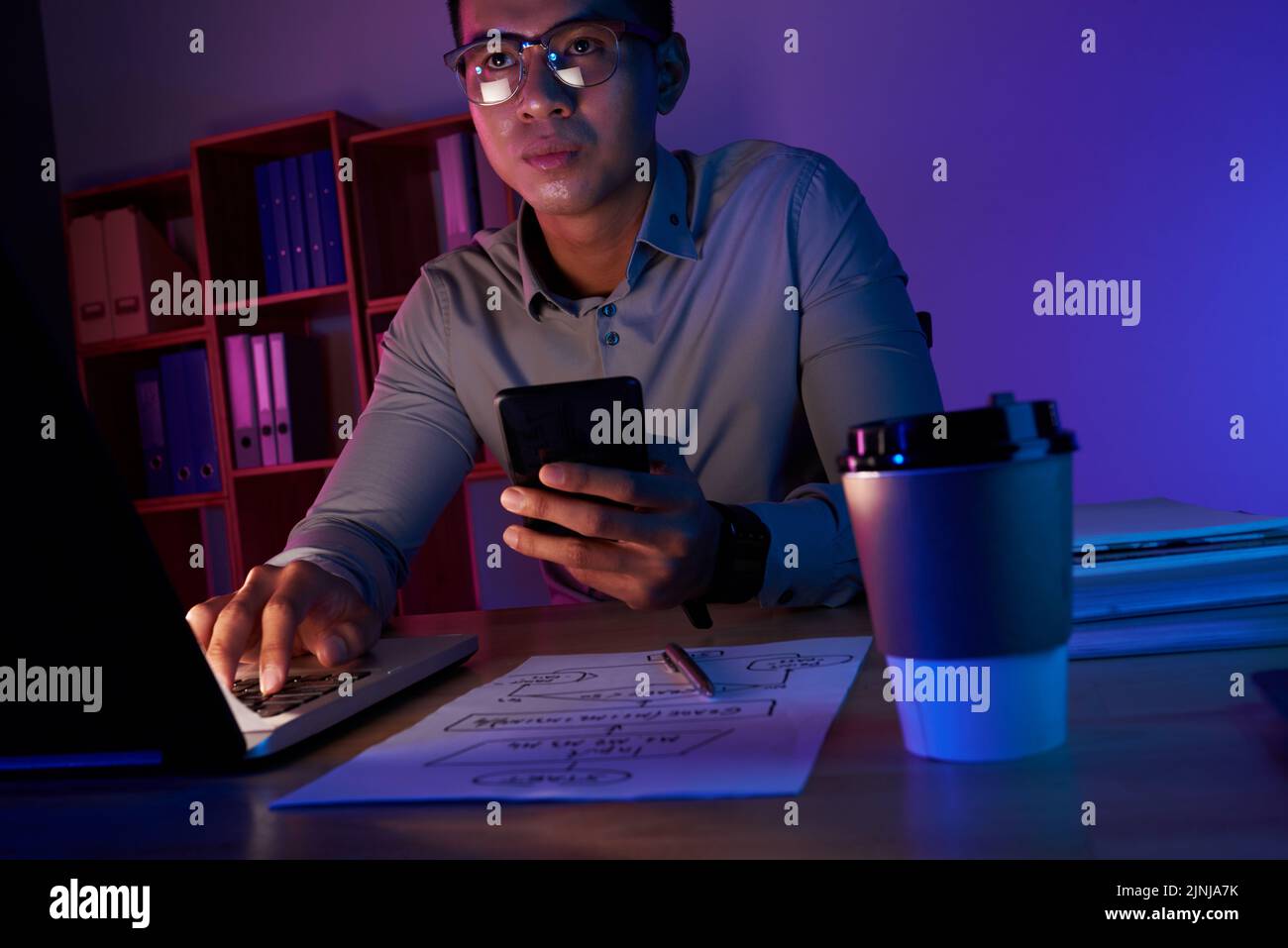 Portrait of concentrated Asian manager in eyeglasses sitting in front ...