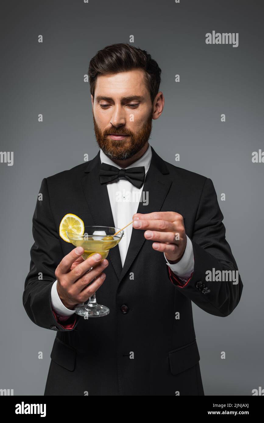 bearded man in suit with bow tie holding toothpick with olive in glass ... bearded man in suit with bow tie holding toothpick with olive in glass ...