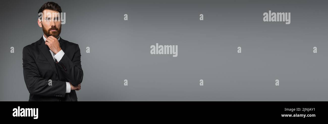 pensive man with beard standing in elegant suit with bow tie looking ...