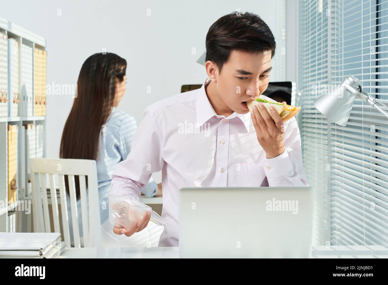 Asian businessman concentrated on work eating sandwich Stock Photo - Alamy