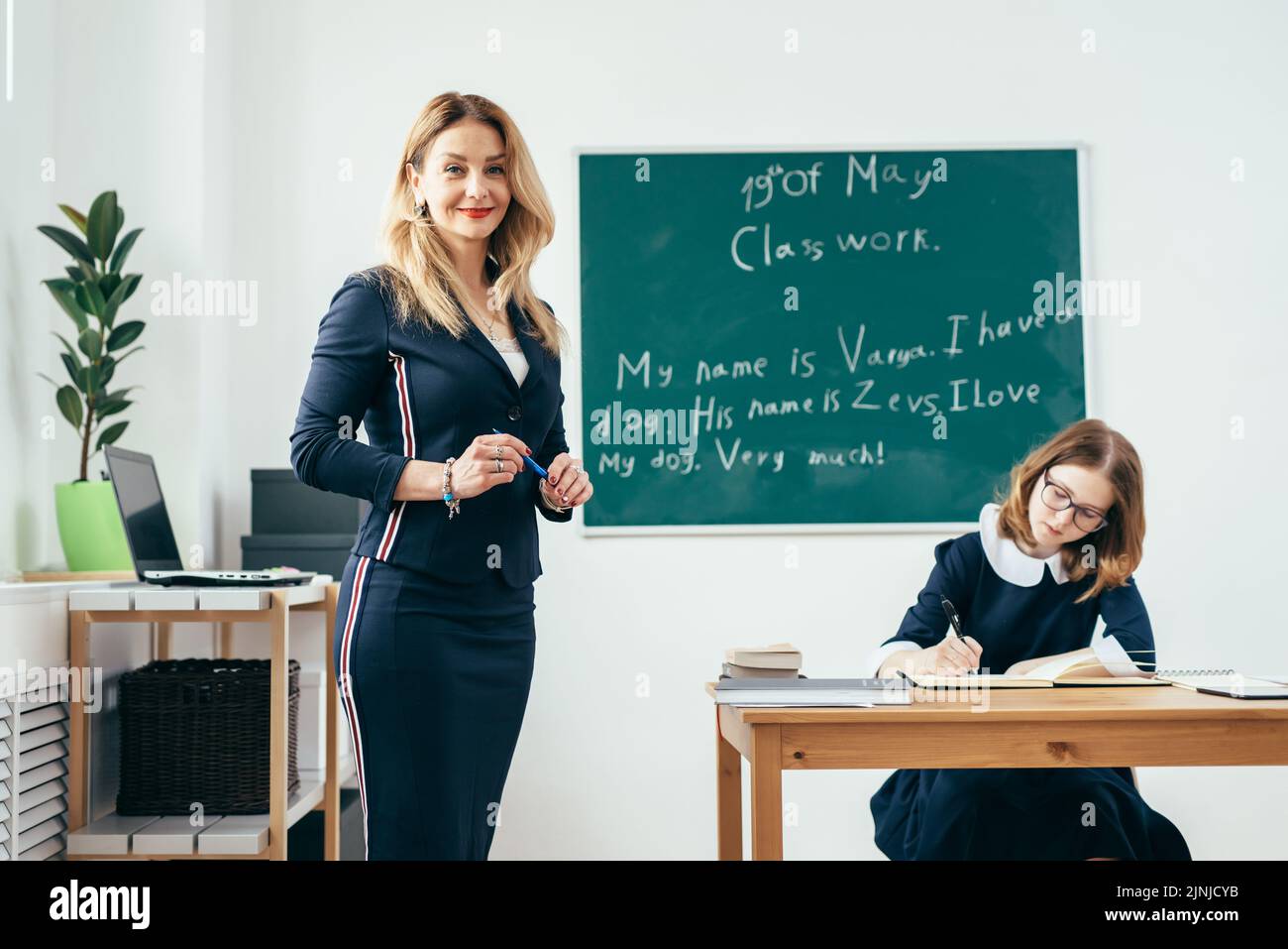 Teacher looking at camera standing in classroom Stock Photo - Alamy