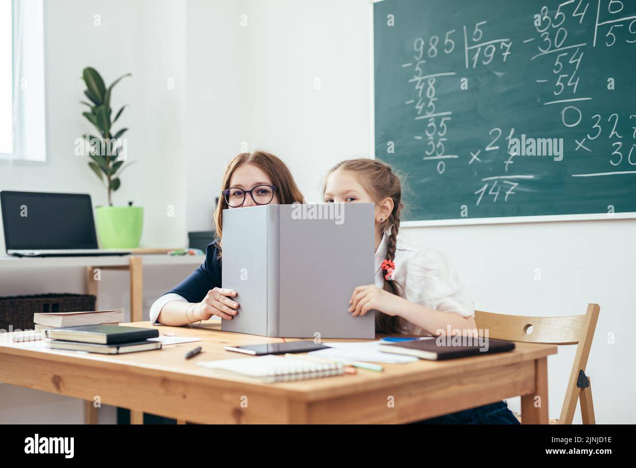 Schoolgirls hiding behind book sitting in a classroom Stock Photo - Alamy
