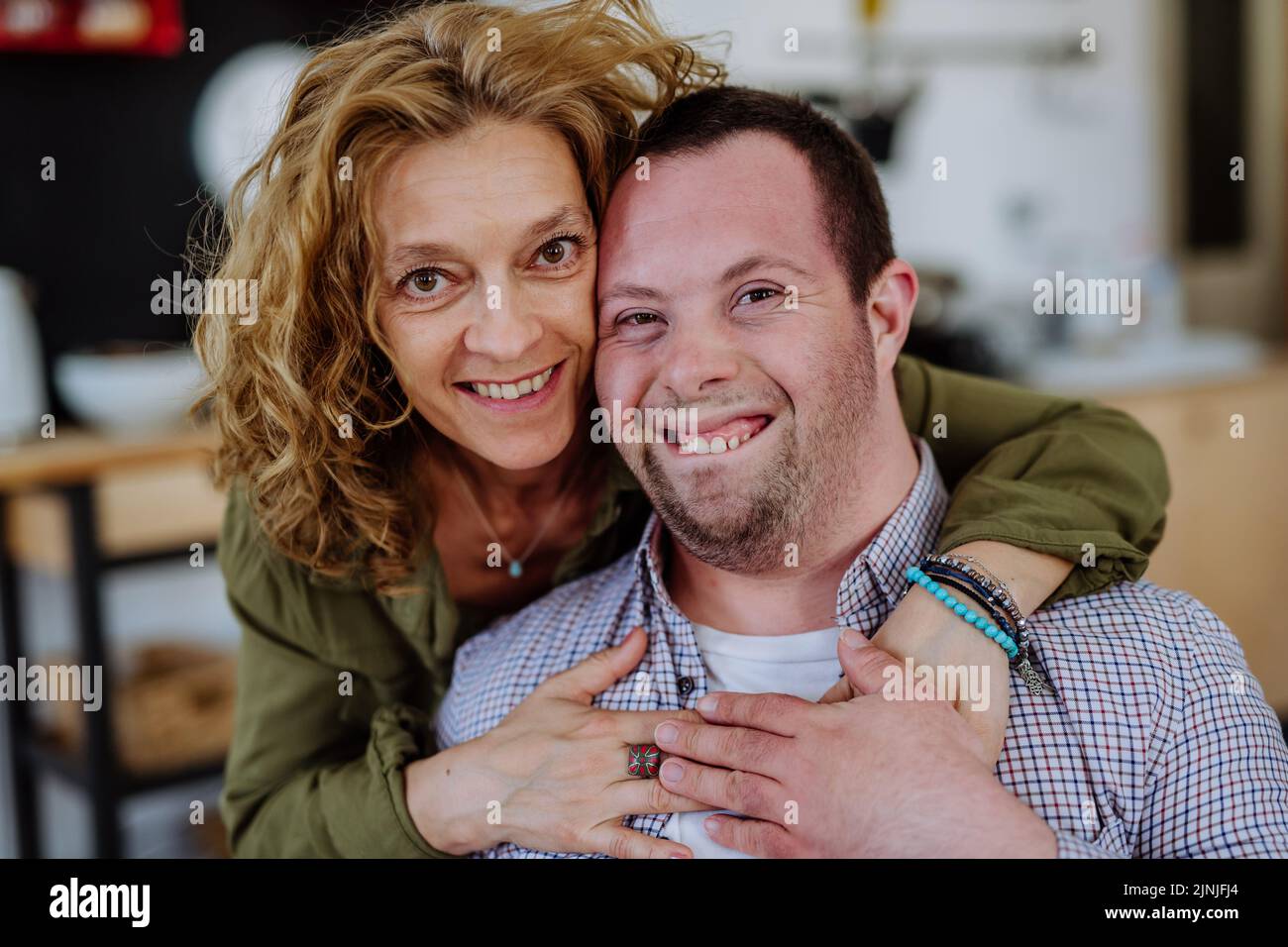 Portrait of mother hugging her grown up son with Down syndrome, motherhood concept. Looking at ...