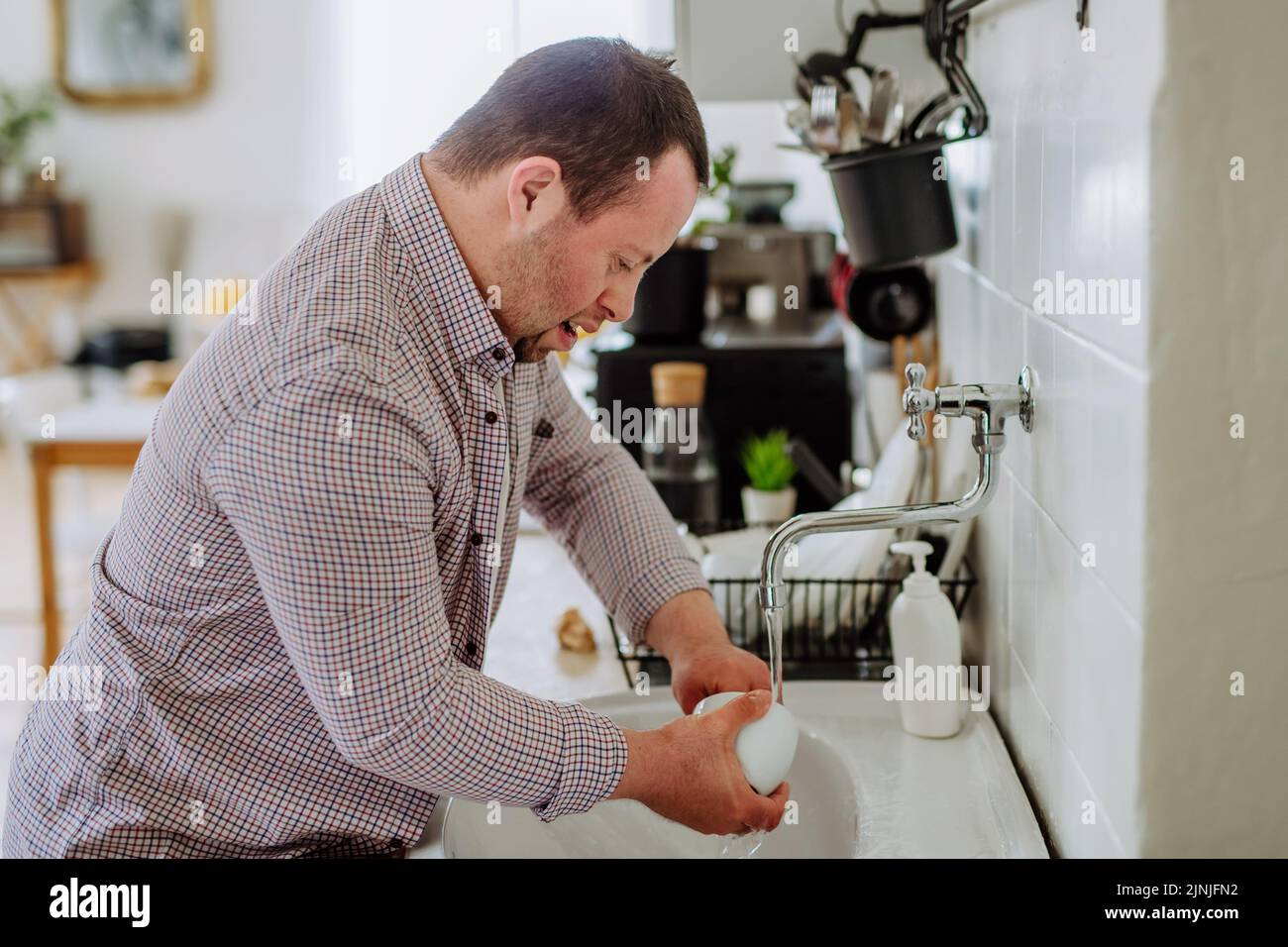Man with down syndrome washing the dishes, taking care of himself ...